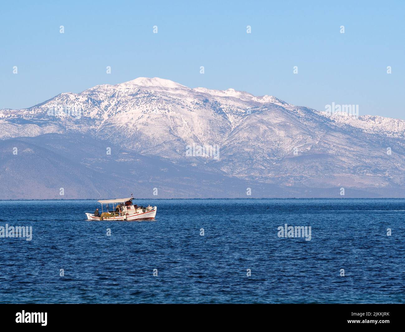A scenic view of a boat sailing in an open sea against a snowy mountain ...