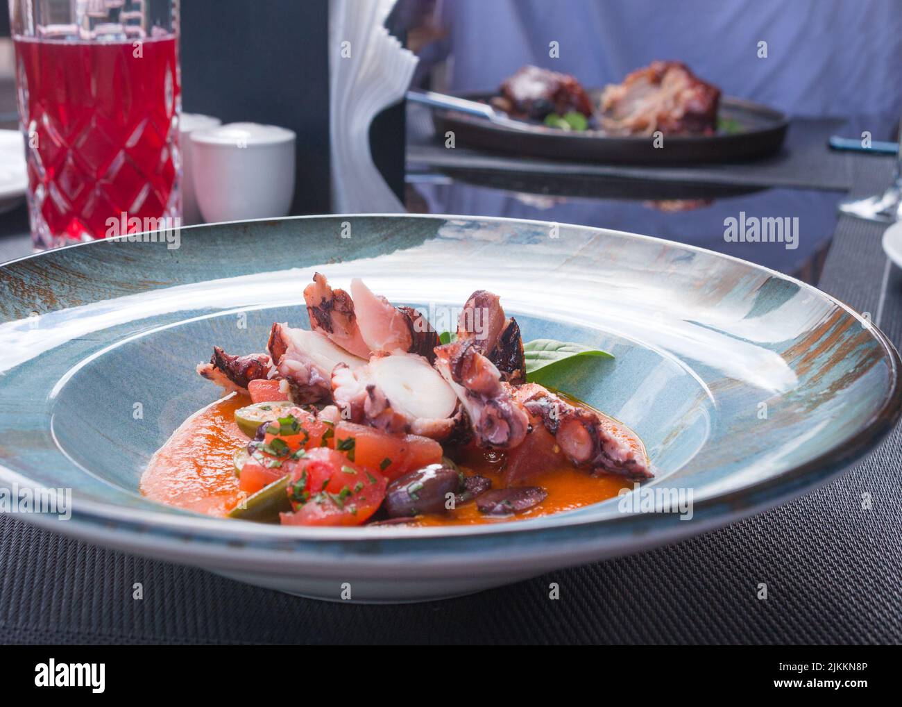 Fried octopus in tomato sauce with olives and capers in a blue plate ...