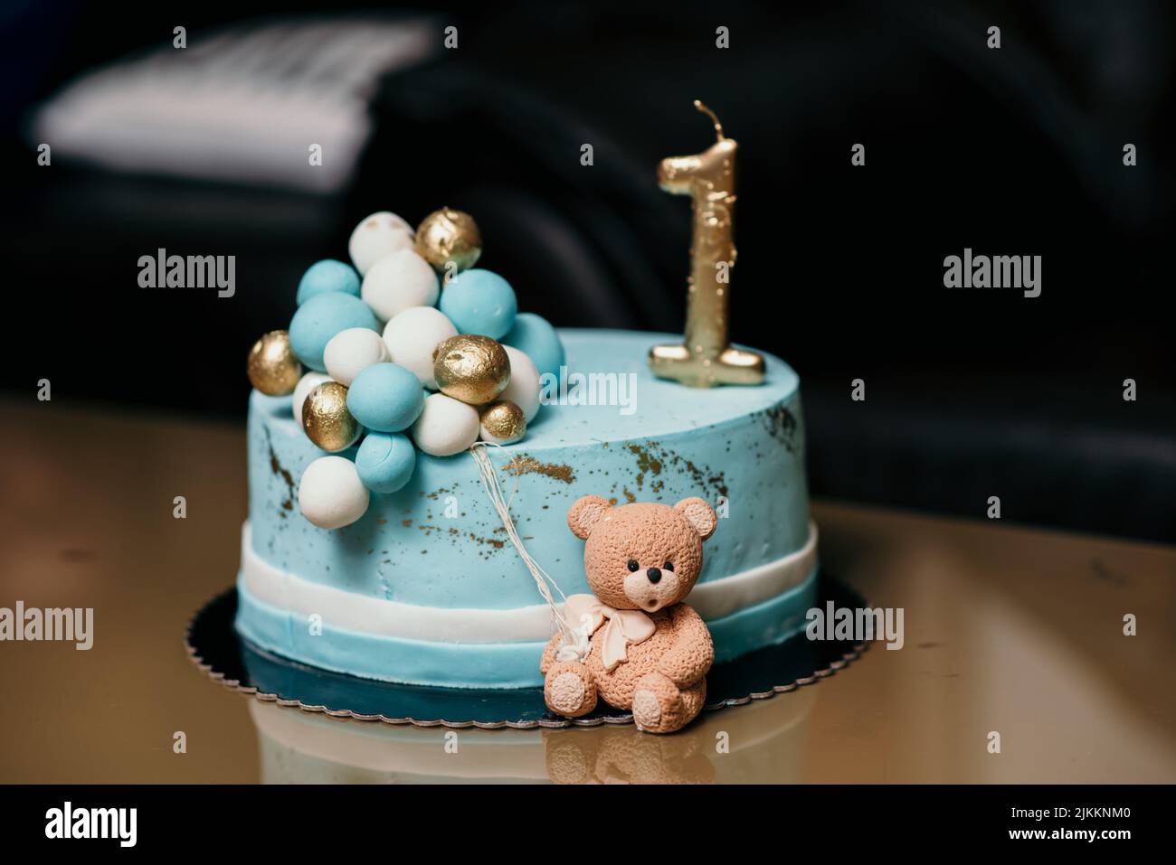 A blue birthday cake with a golden, number one candle, decorated with a ...