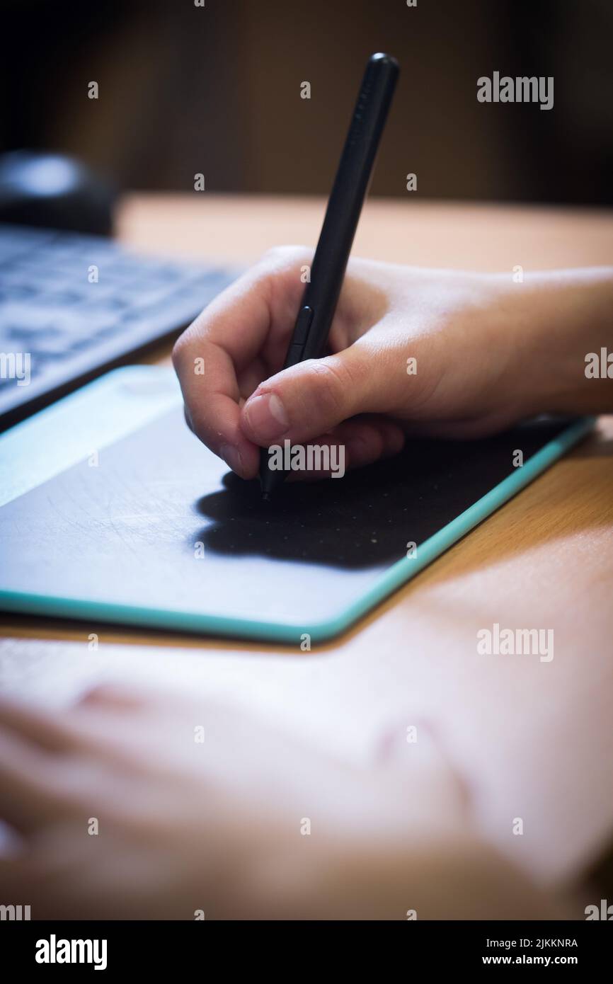 A vertical shot of a hand drawing on a graphic design tablet with a ...