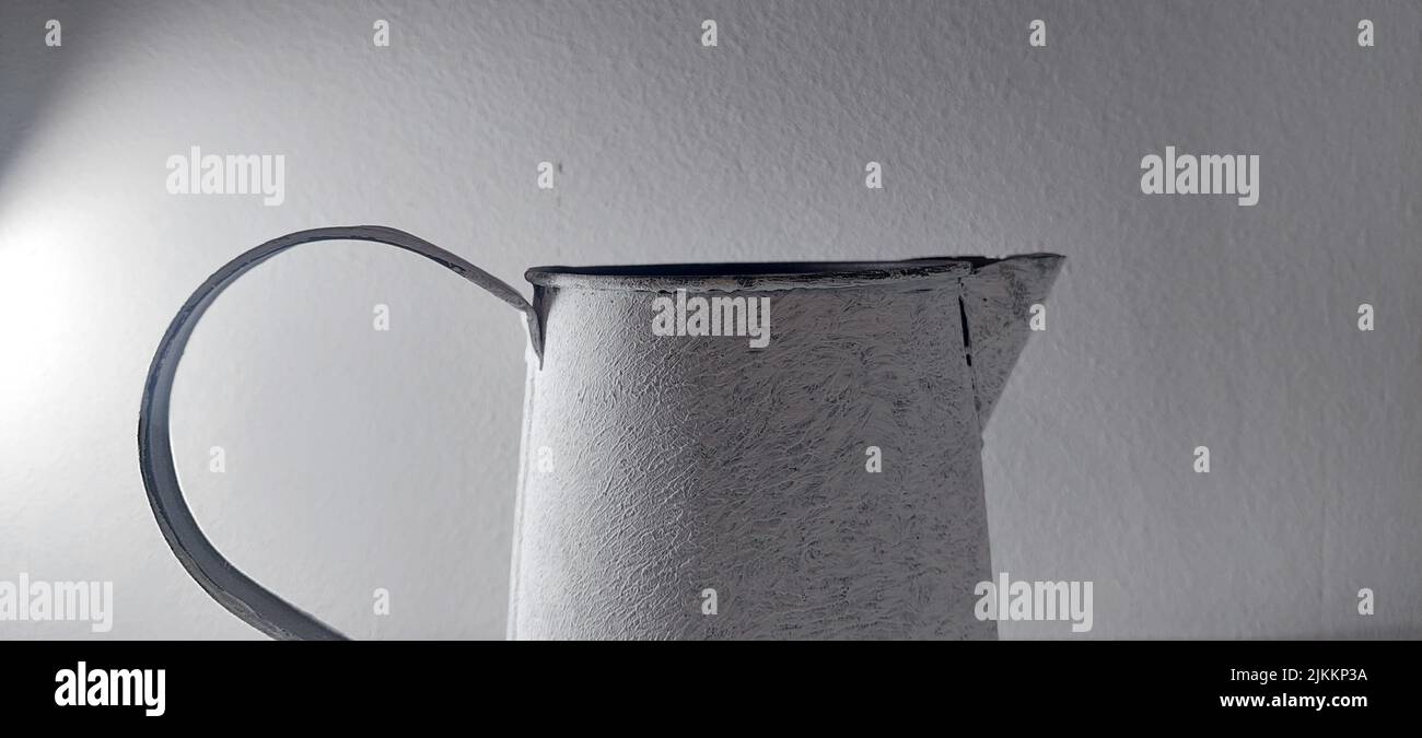 A grayscale shot of a white, iron jug with a background of white wall ...