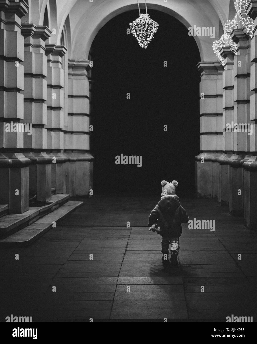 A vertical grayscale shot of a little kid inside a building with ...