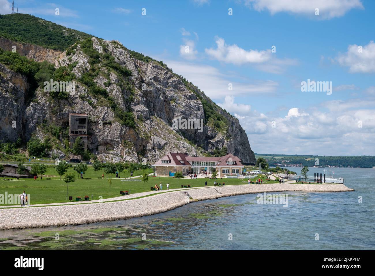 A scenic waterfront landscape with a building, people, a lawn, and ...