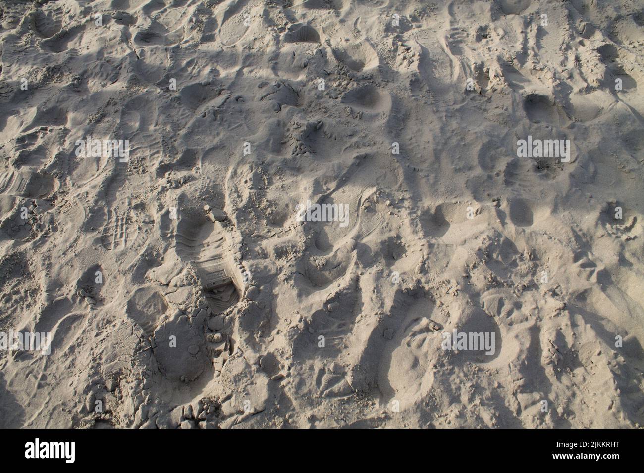A top view of footprints imprinted on the sand at a beach with shadows ...