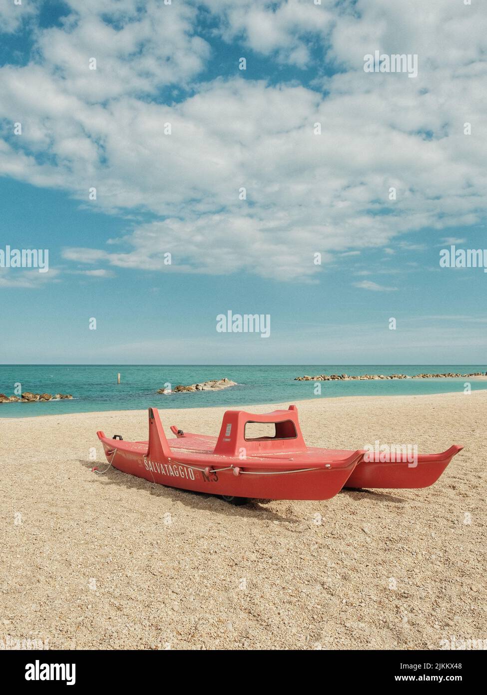 A vertical shot of a red lifeguard boat on the sandy beach near the ...