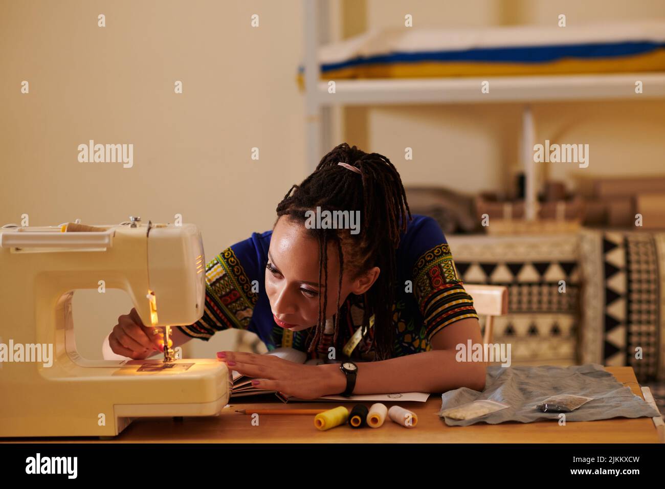 Seamstress threading sewing machine needle when working in her studio ...