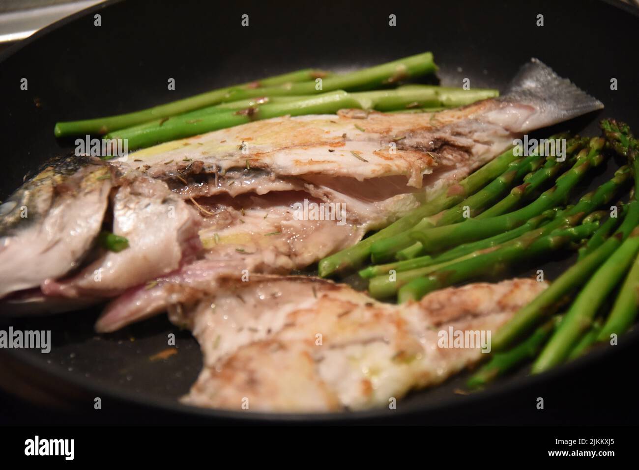 A fish with asparagus on a frying pan Stock Photo - Alamy