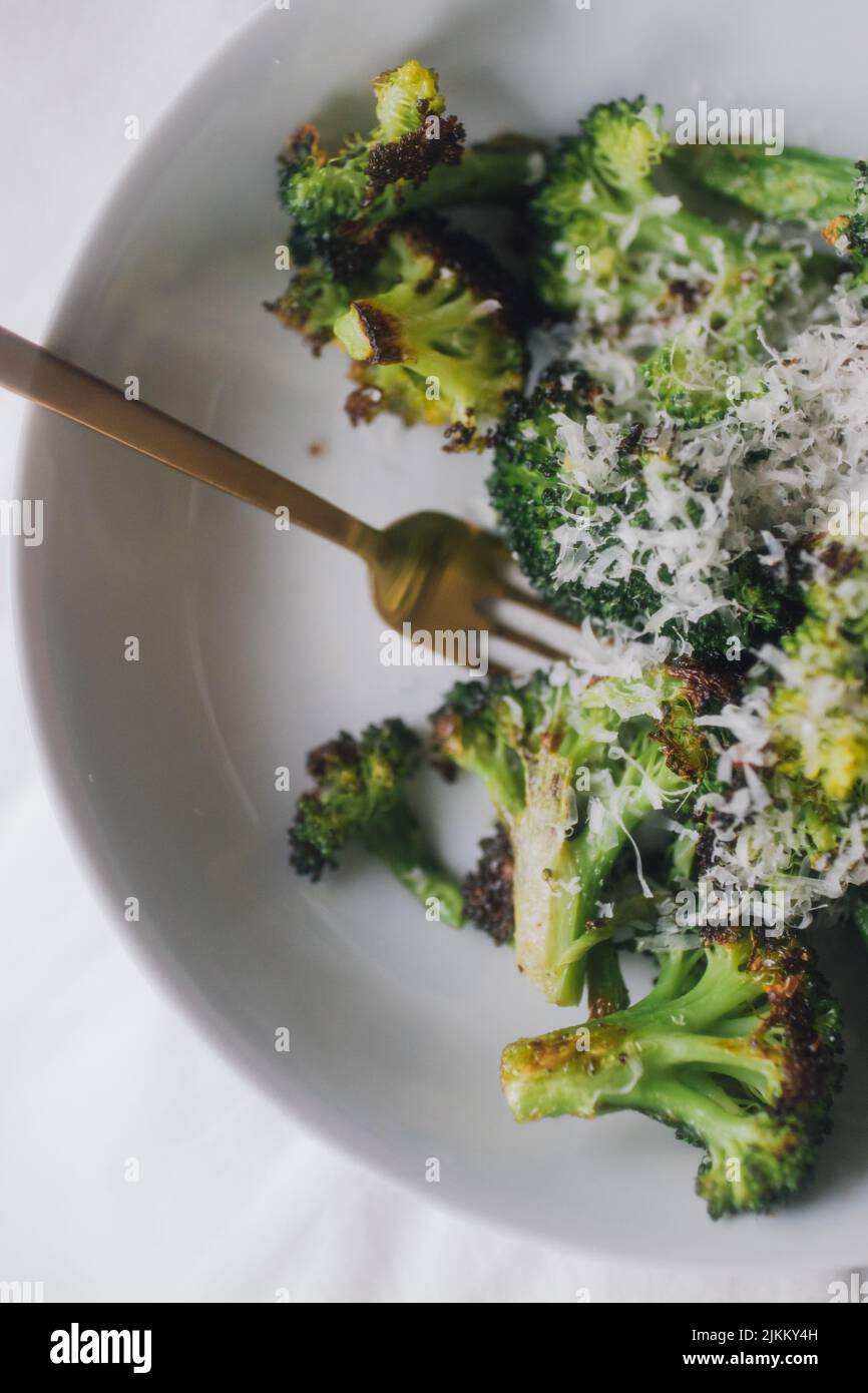 roasted broccoli with parmesan cheese on white dish with gold fork ...