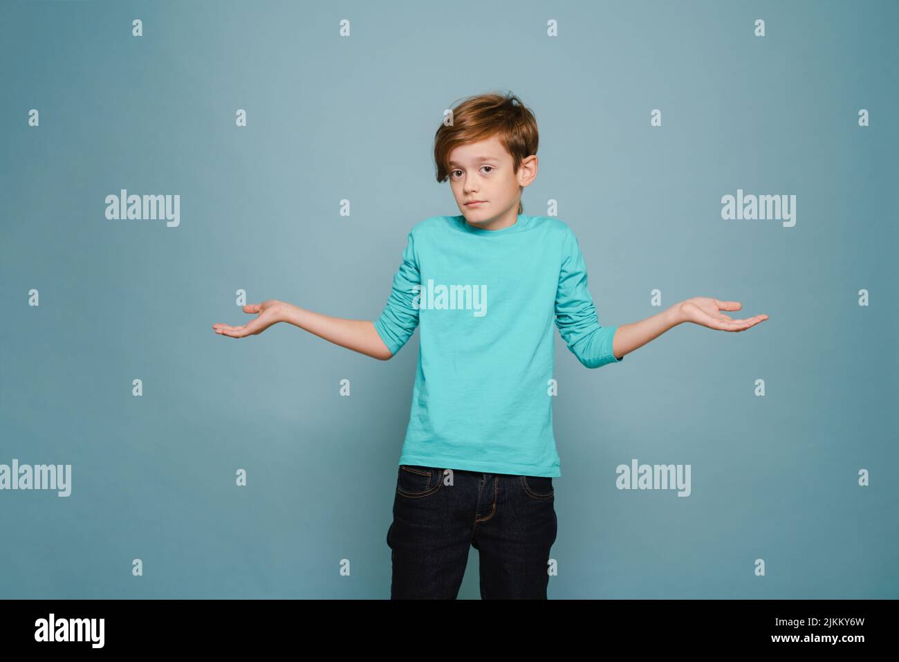 Ginger perplexed boy gesturing and looking at camera isolated over blue ...