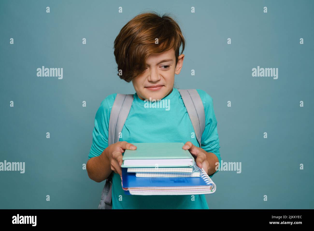 Ginger displeased boy with backpack posing with exercise books isolated ...