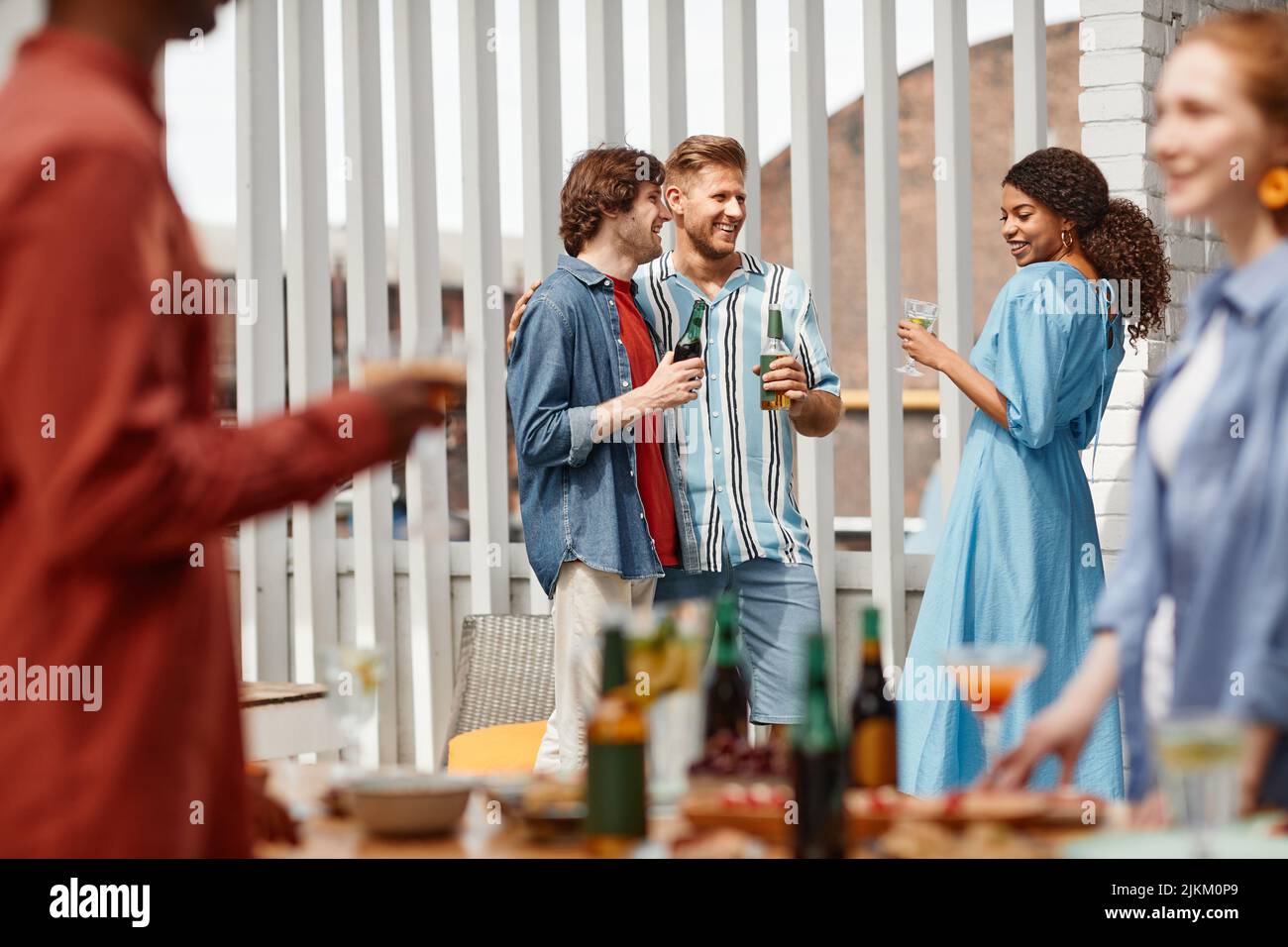 Diverse group of friends enjoying party outdoors at terrace lit by ...