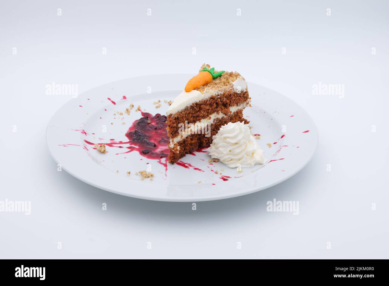 A closeup of a carrot cake with creamy topping on a plate on a white ...