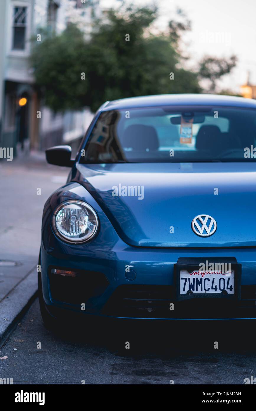 A vertical shot of a blue Volkswagen Beetle parked by a sidewalk Stock ...