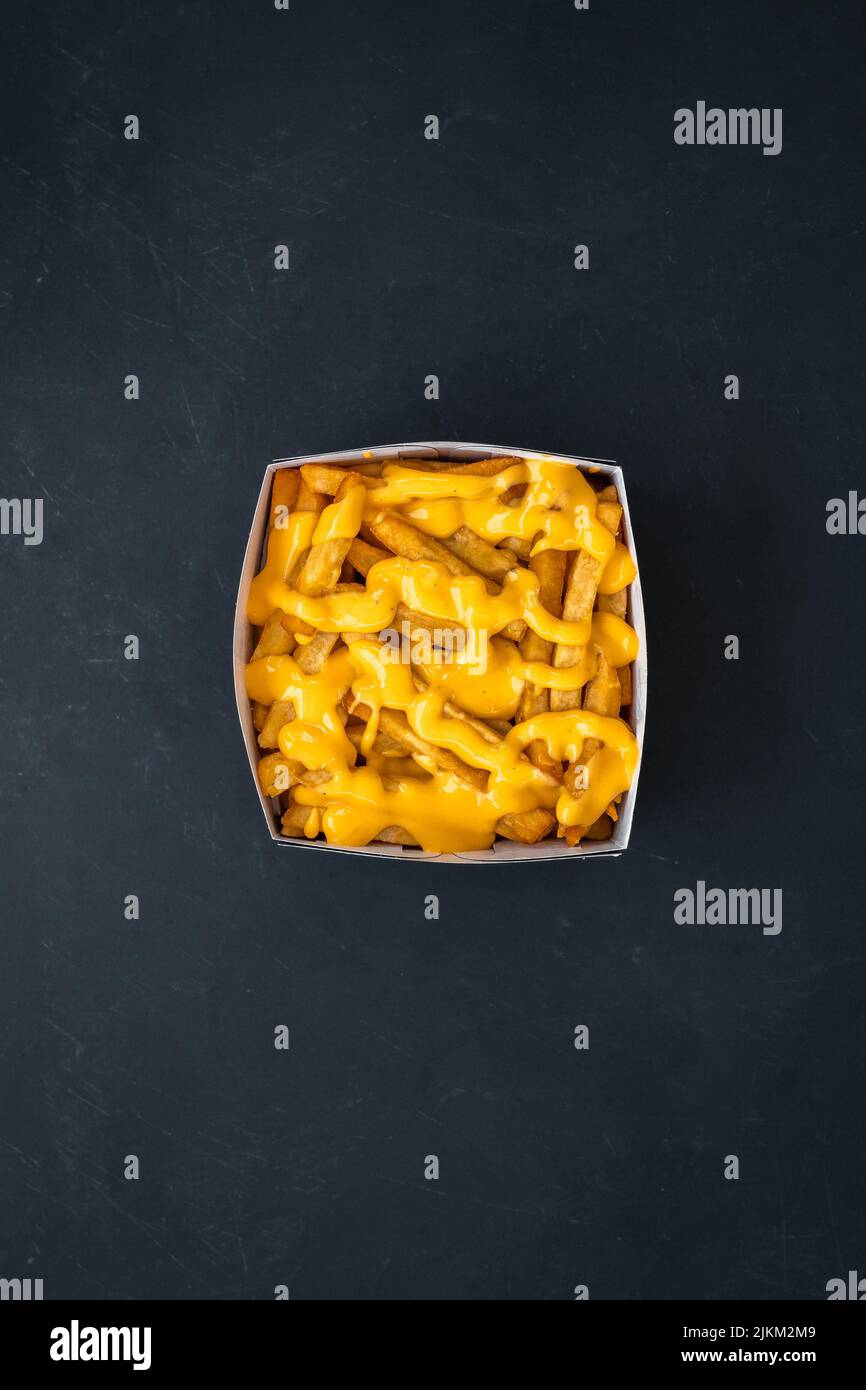 A vertical top view of a container of delicious cheesy fries on a gray ...