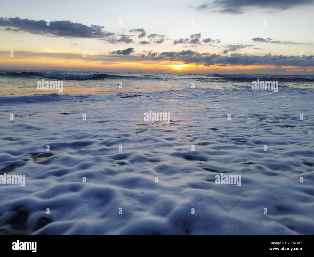 A beautiful shot of sunset over the foamy waves hitting the shore of ...