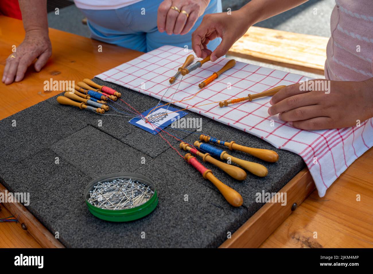 Hands making bobbin lace. Adult helps child learn craft. Colorful lace ...