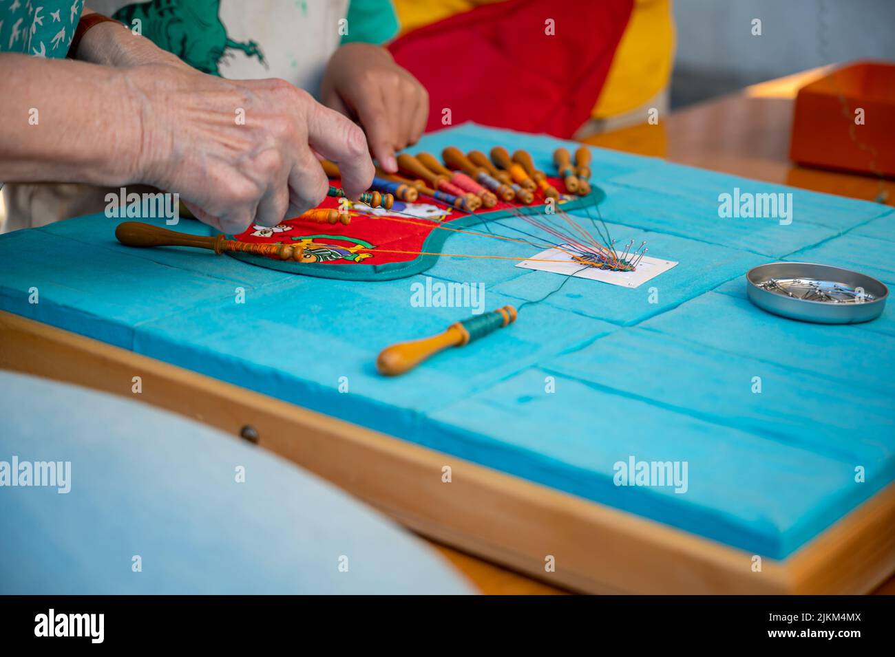 Hands making bobbin lace. Adult helps child learn craft. Colorful lace ...