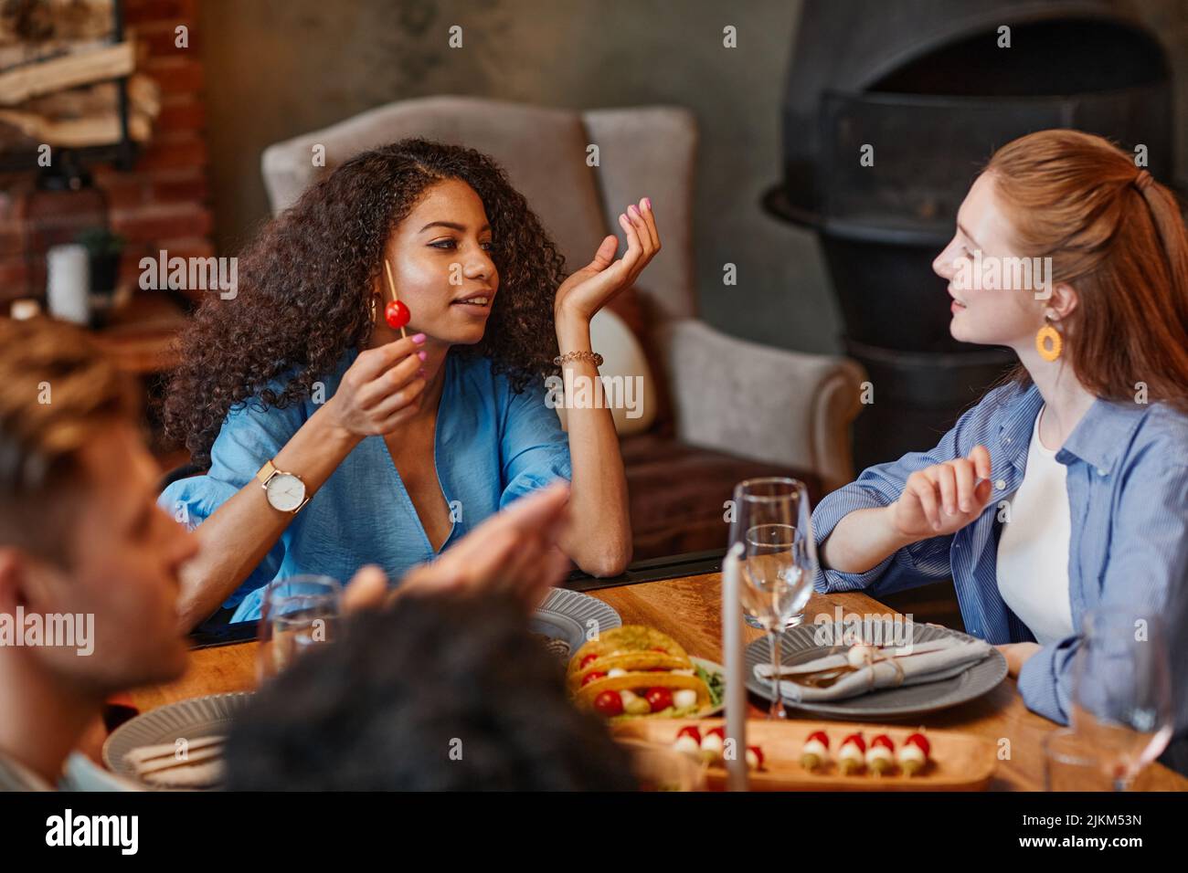 Portrait of young black woman talking to friends at table during dinner ...