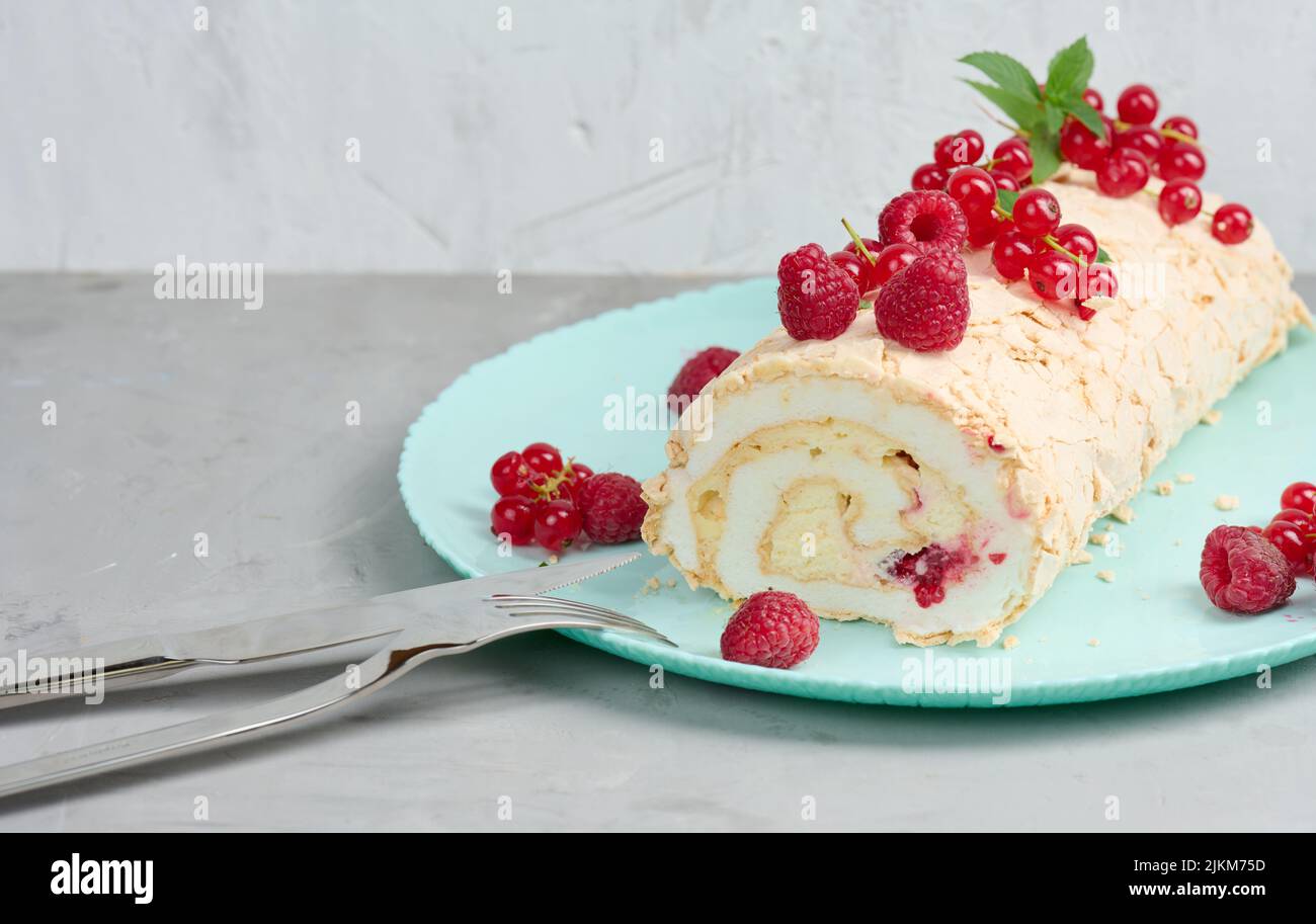 Baked meringue roll with red berries on a round plate, white background ...