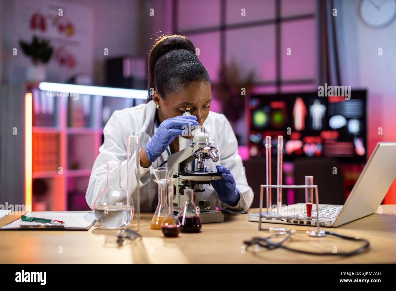 Young african female researcher looking at the microscope observing ...