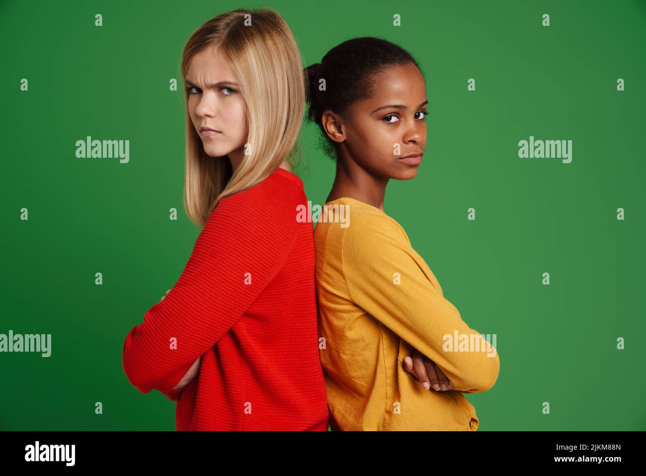 Multiracial two girls posing back to back on camera isolated over green ...