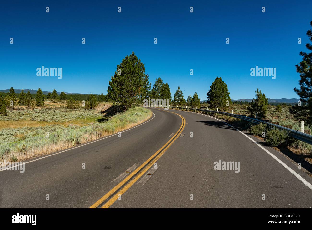 Two lane road bends into a meadow in the Sierra Nevada Mountains of ...