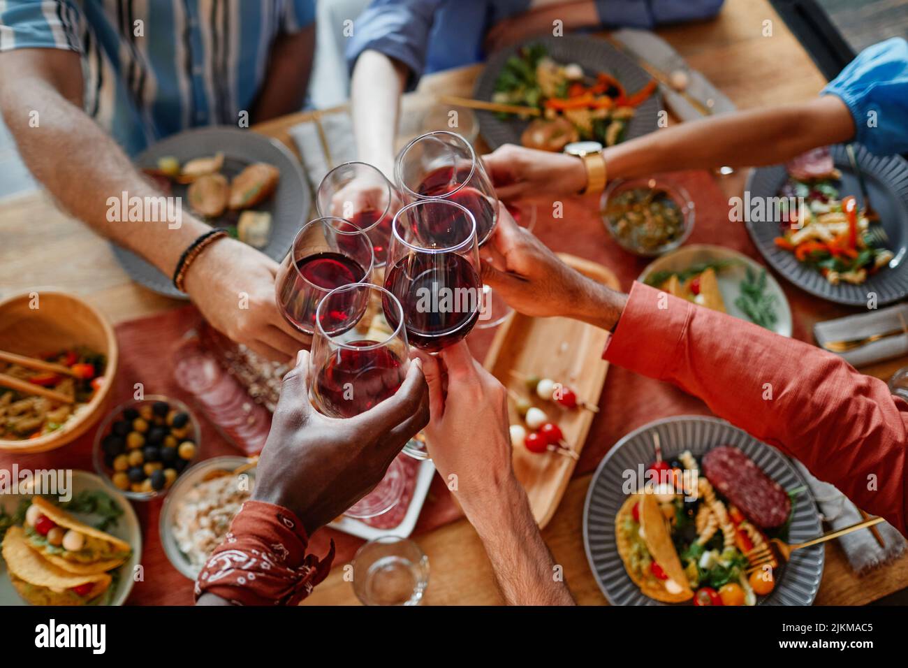 Top down view of young people toasting with wine glasses while ...