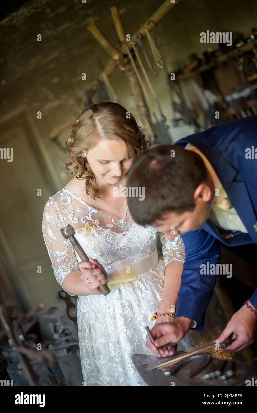 A caucasian bride and groom at a blacksmith hitting metal and engraving ...
