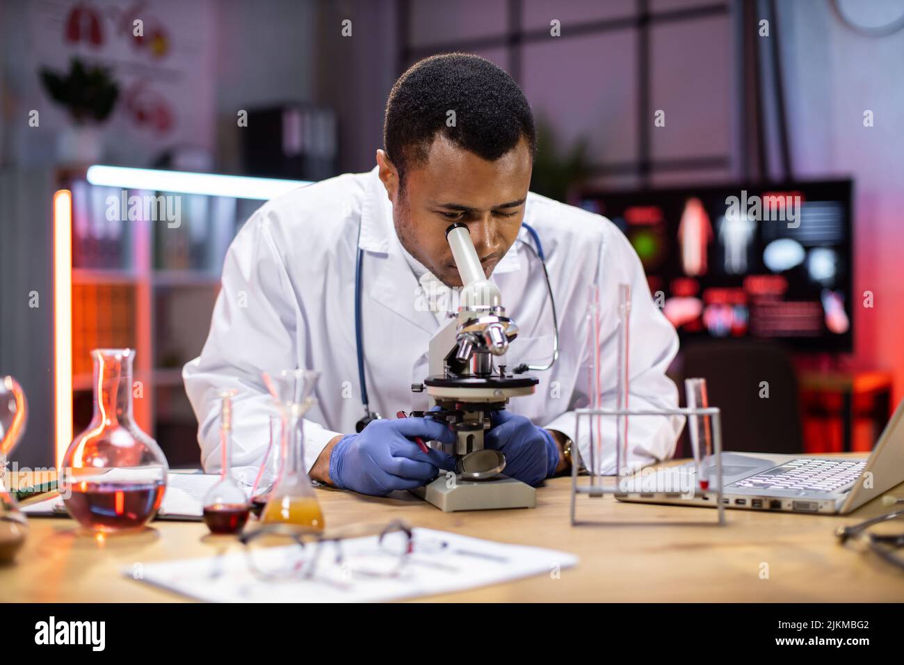 Young african american male researcher looking at the microscope ...