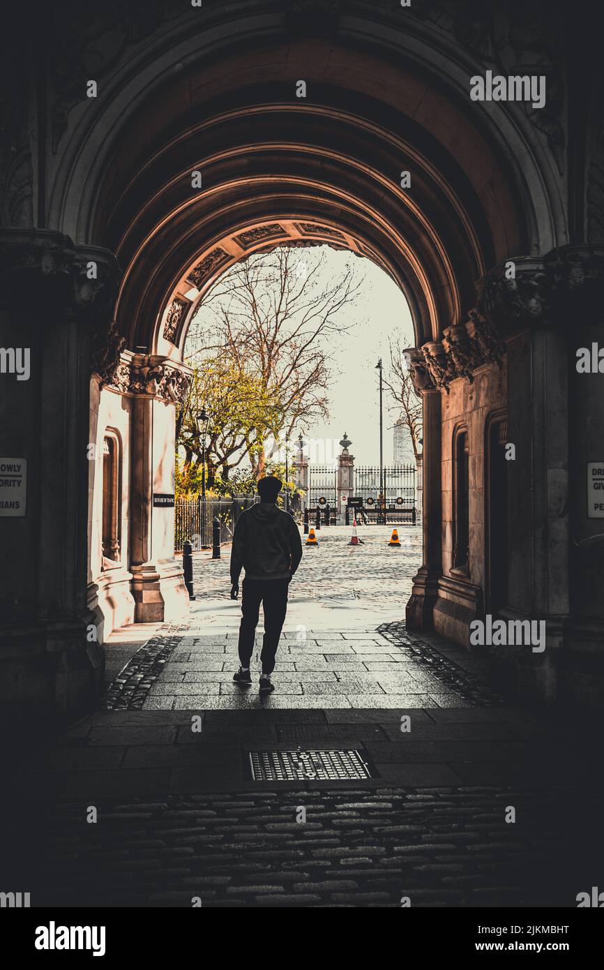 A vertical shot of a person standing in front of an arch of a central ...