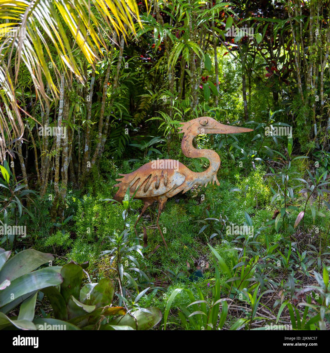 A closeup of a rusted metal heron statue surrounded by lush greenery in ...
