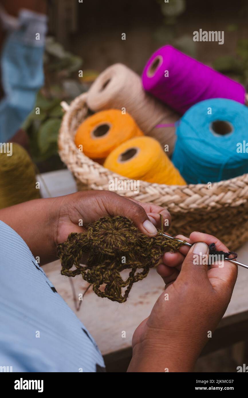A vertical shot of the hands knitting a decoration and colorful threads ...