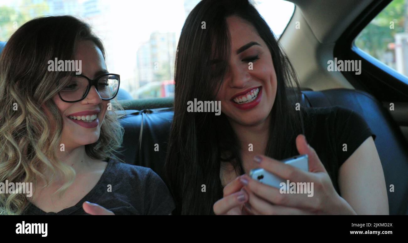 Candid Girlfriends In The Back Seat Of A Car Sharing Cellphone Screen Showing Content Friends