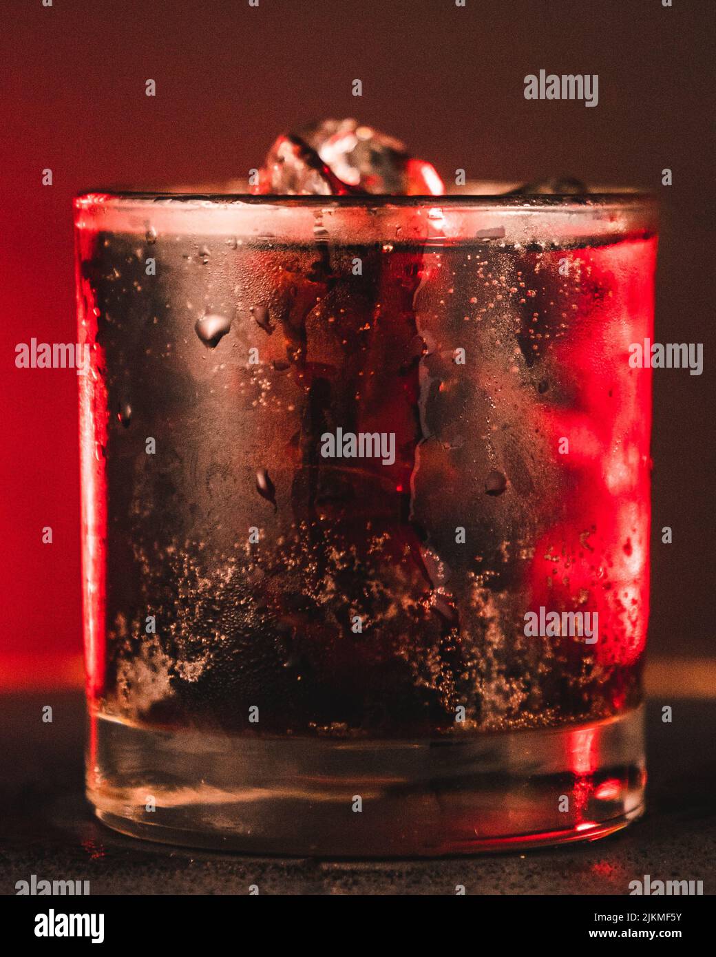 A vertical closeup of a soda drink with ice cubes in it against a red ...