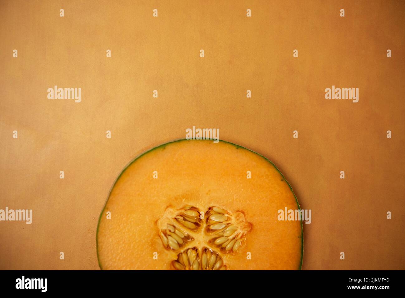 Single cantaloupe slice on terracotta orange background top view half ...