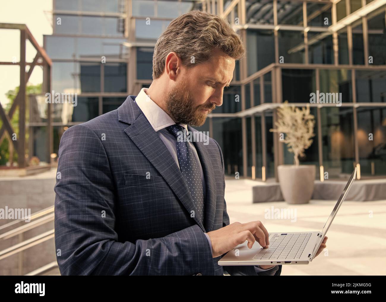 entrepreneur in businesslike suit typing on pc outside the office ...