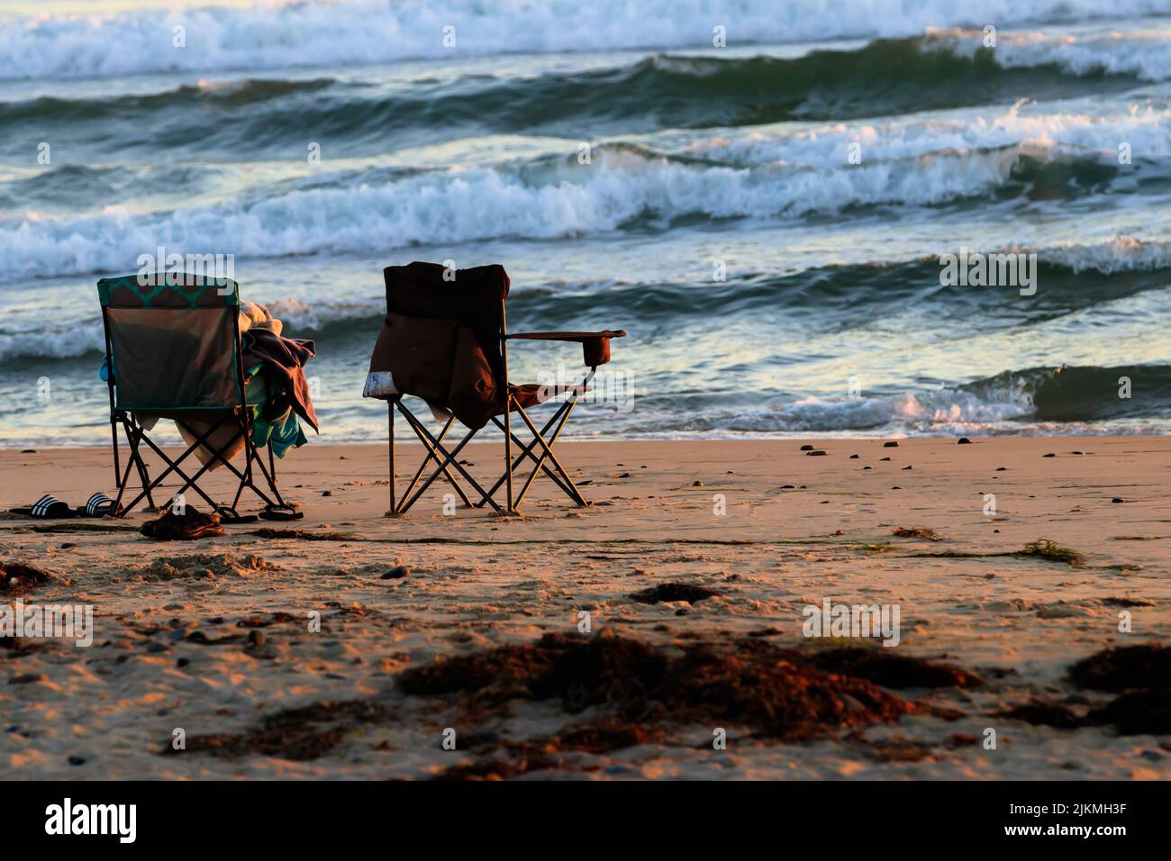 A scenic view of the wavy beach with two chairs isolated on the sand ...