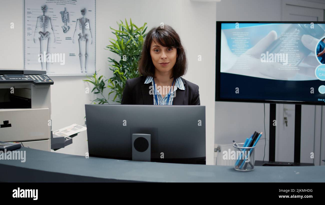 Portrait of receptionist working at hospital reception desk to help people with appointment for ...