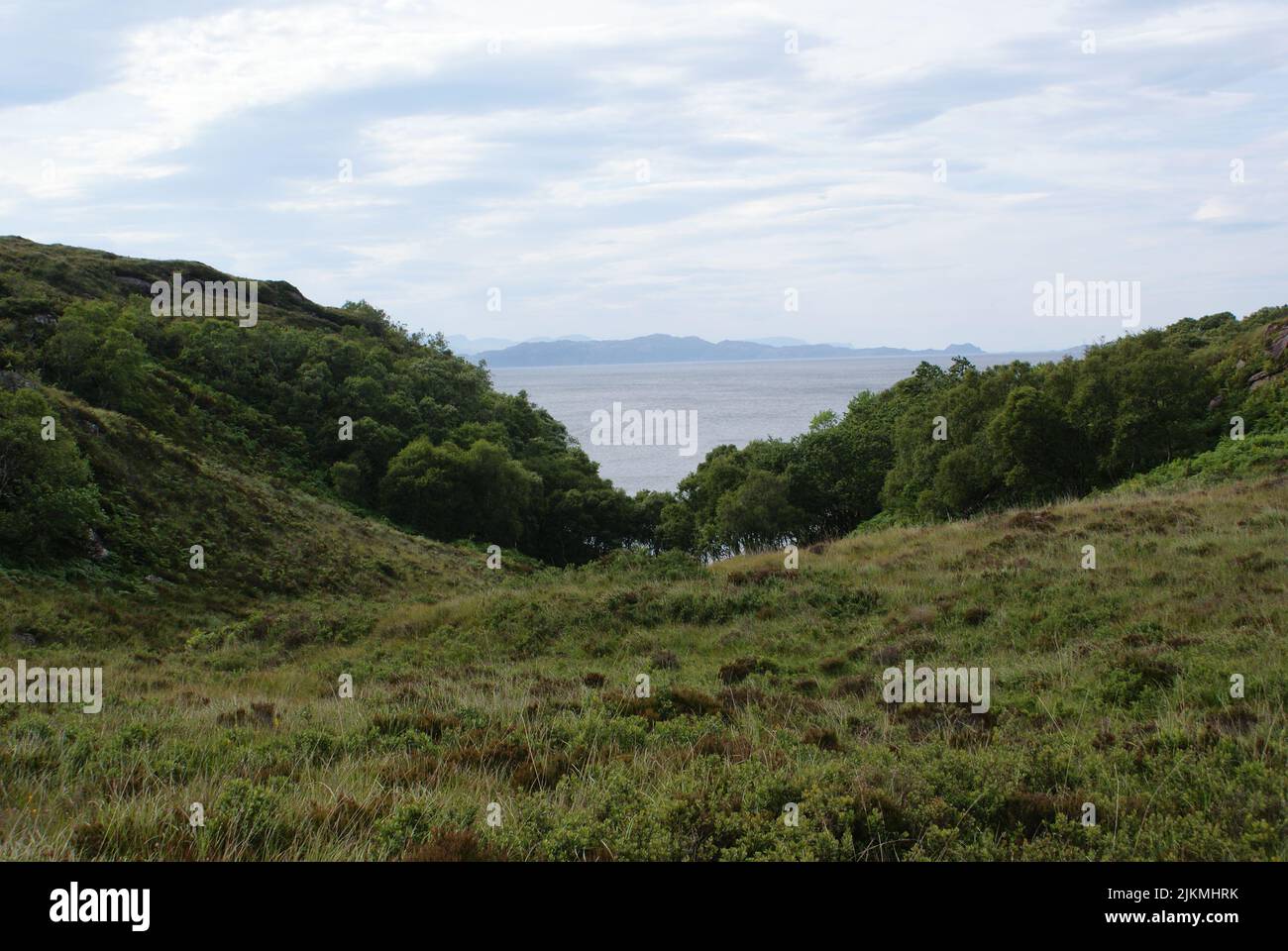 A scenic view of grassy terrain under a cloudy sky with sea background ...