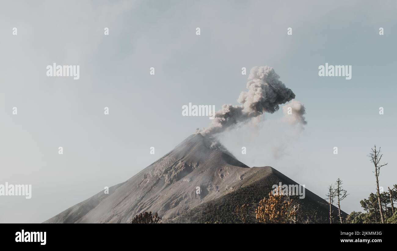 A volcano with dark smoke coming from it under a pale sky in Antigua ...