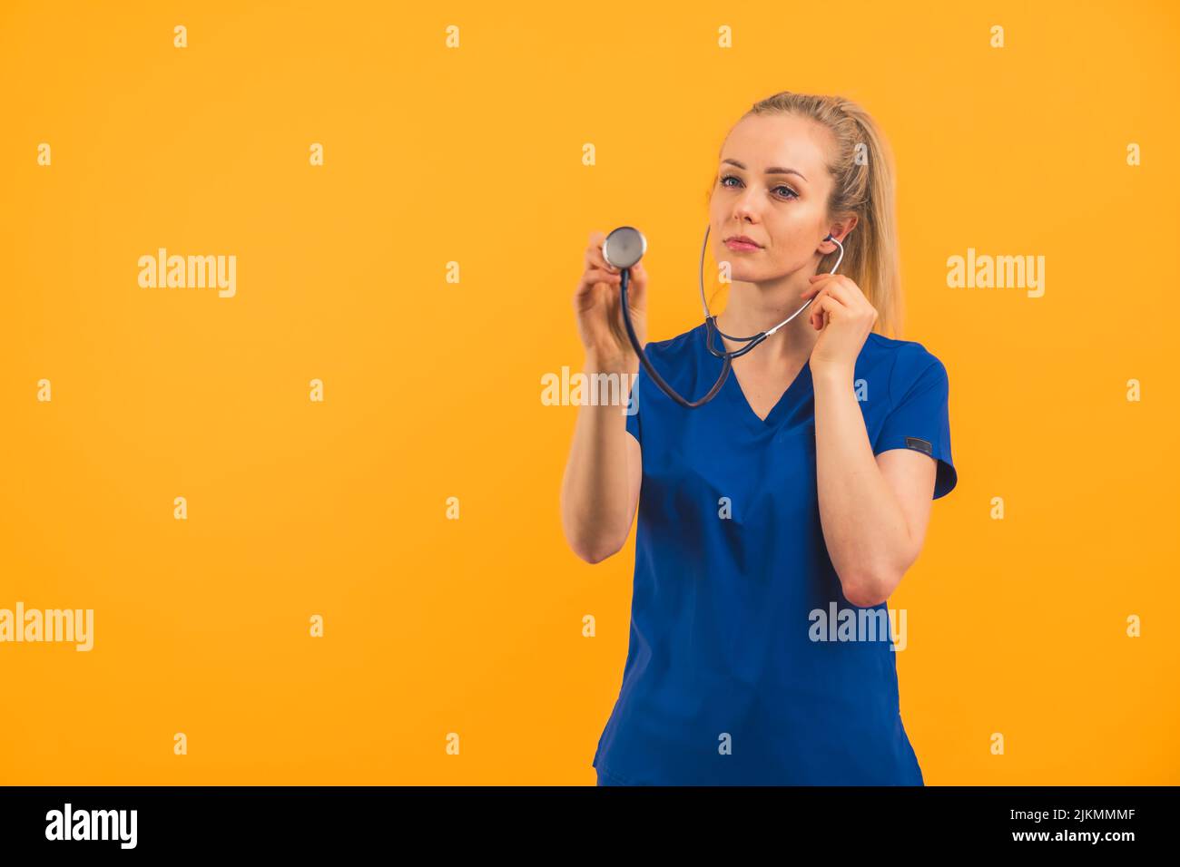 a blonde caucasian nurse in blue using a Stethoscope - closeup orange ...