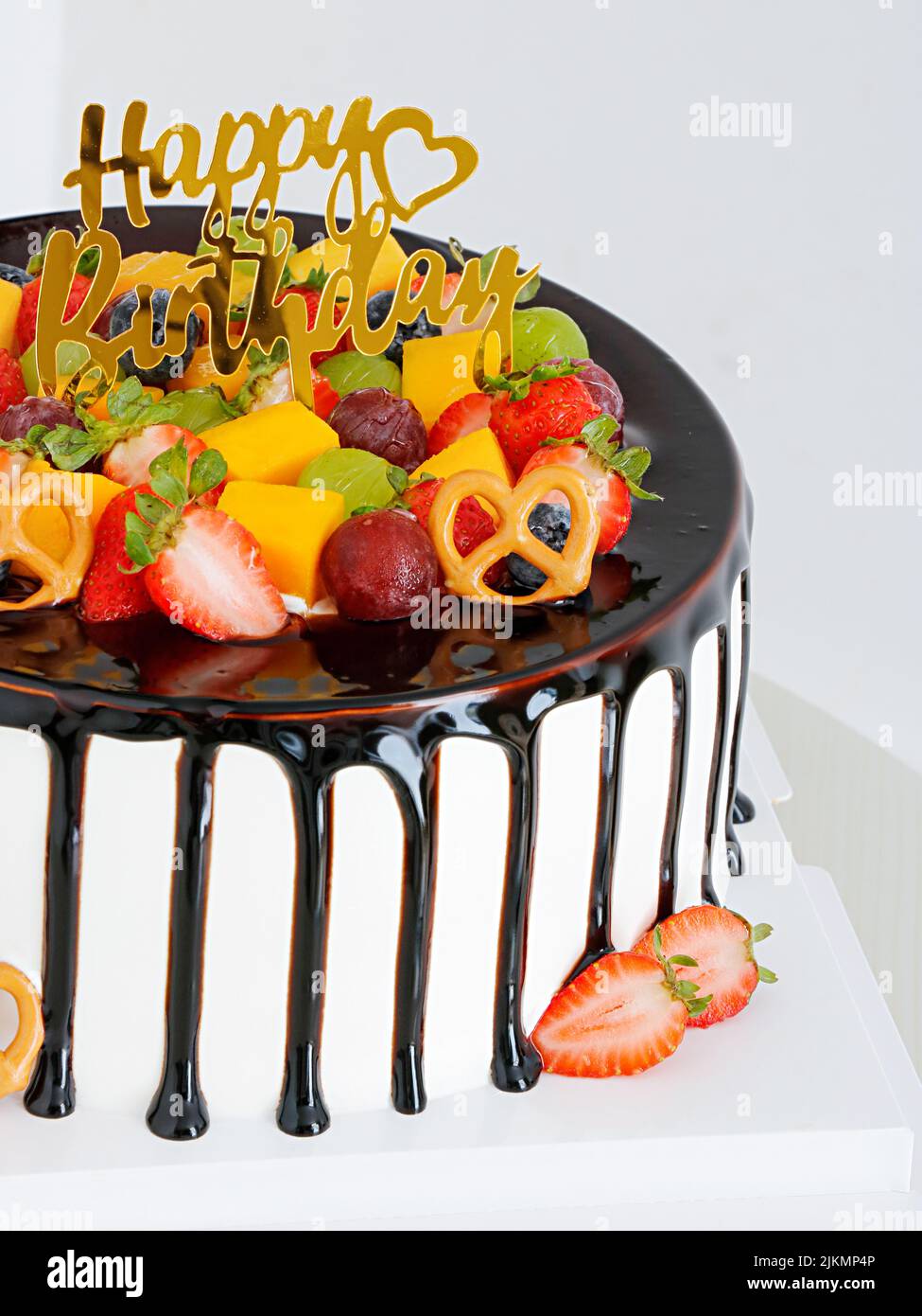 A Cake with chocolate syrup,fruits and a happy birthday sign on a white ...