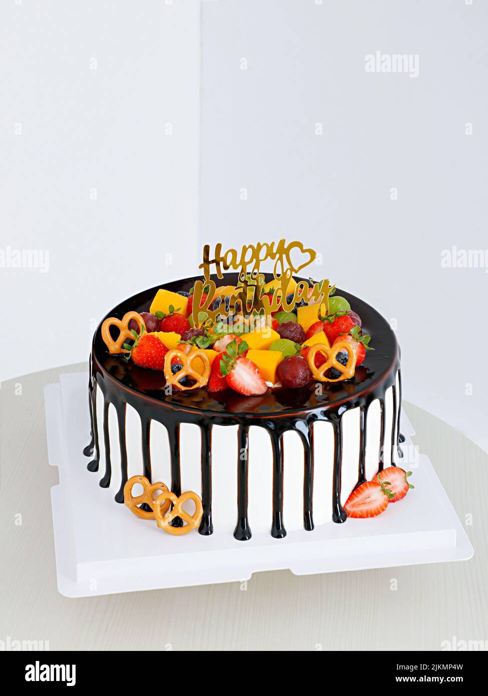 A Cake with chocolate syrup,fruits and a happy birthday sign on a white ...