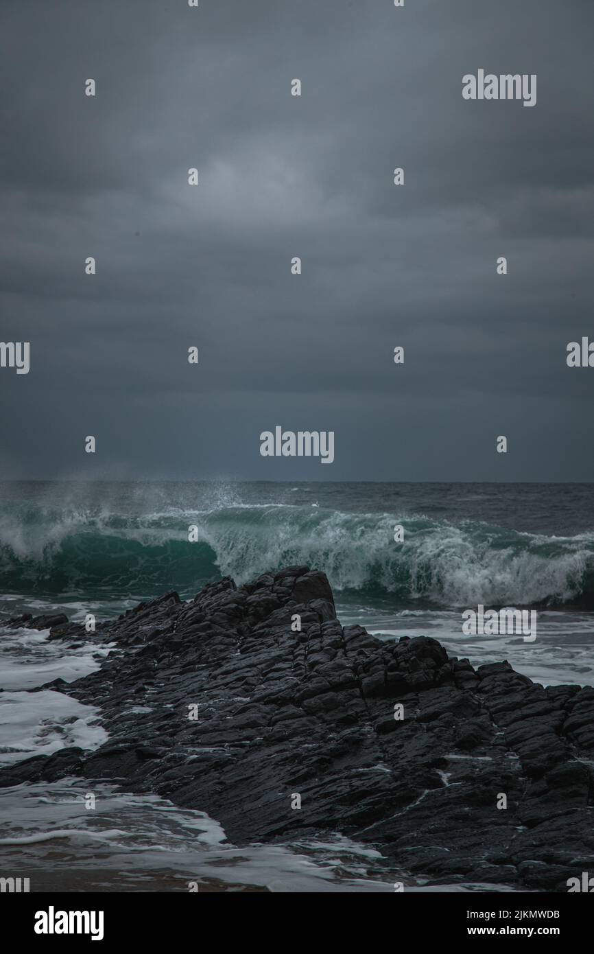 A vertical shot of a sea storm with splashing waves and rocks under a ...