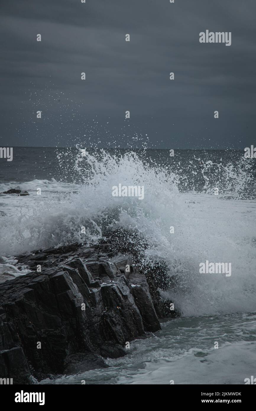 A vertical shot of a sea storm with splashing waves and rocks under a ...