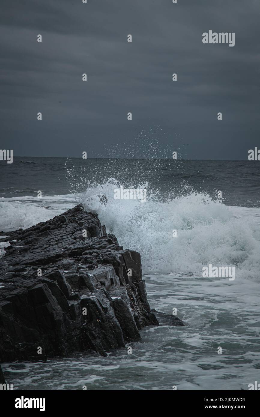 A vertical shot of a sea storm with splashing waves and rocks under a ...