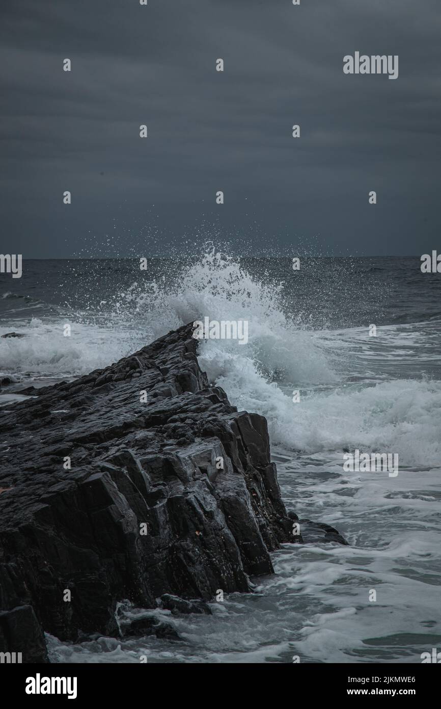 A vertical shot of a sea storm with splashing waves and rocks under a ...