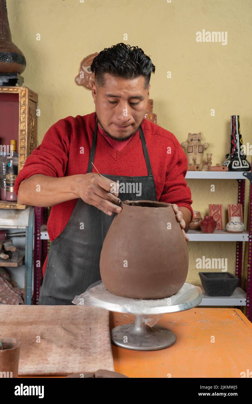 Vertical image of a potter using a small stick to make a ceramic vessel ...