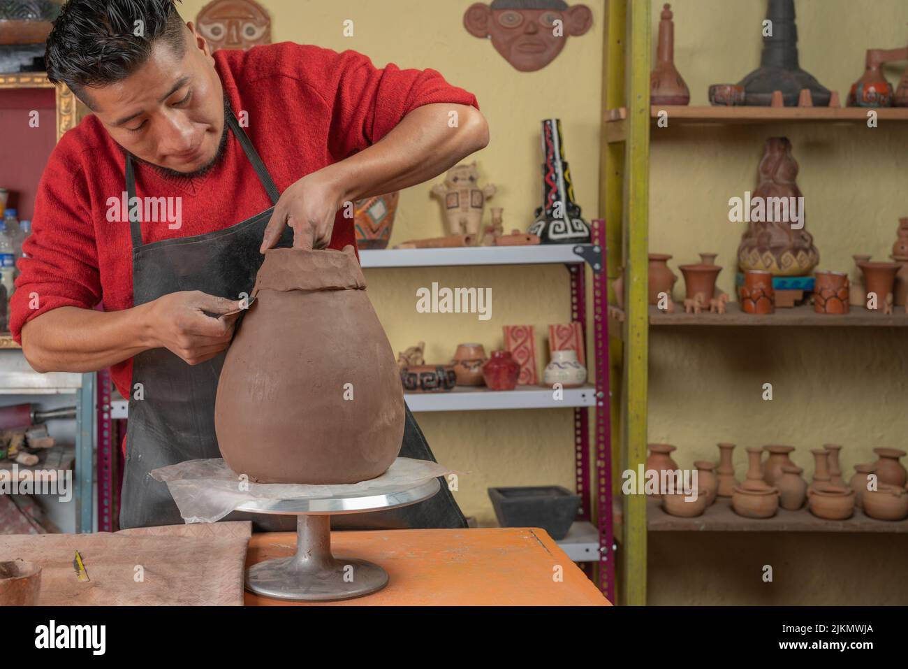 Potter making and shaping a pottery vessel with a tool in his workshop ...