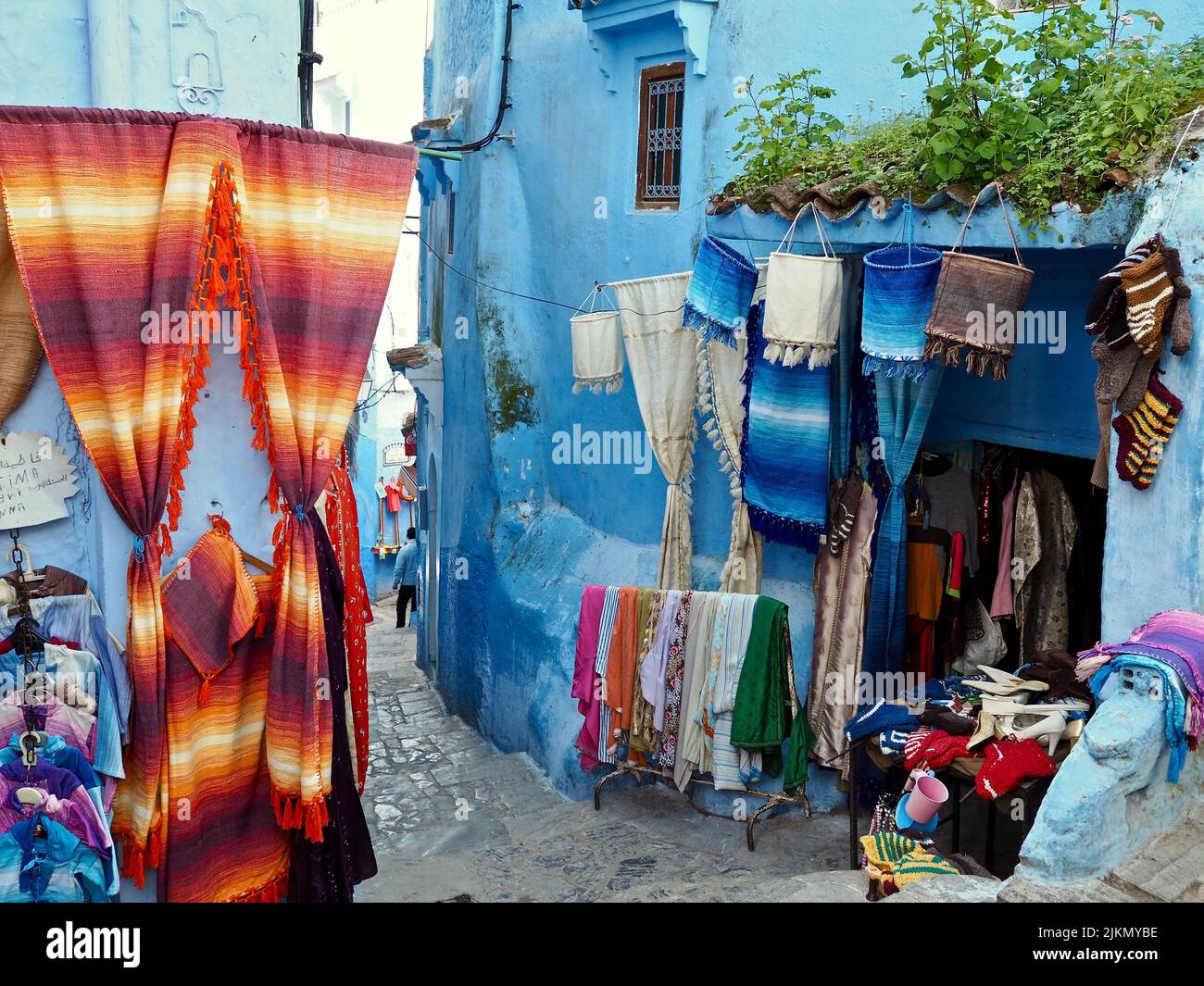 A narrow street with buildings and a shop with textile objects hanging ...